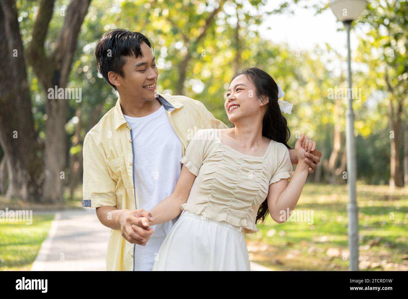 A lovely young Asian couple is dancing in a beautiful green park ...