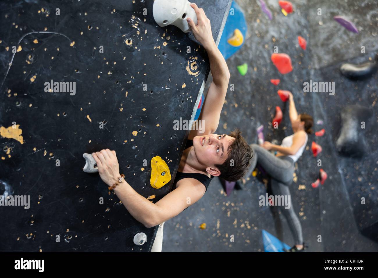 Positive focused young guy exercising on black climbing wall without ...