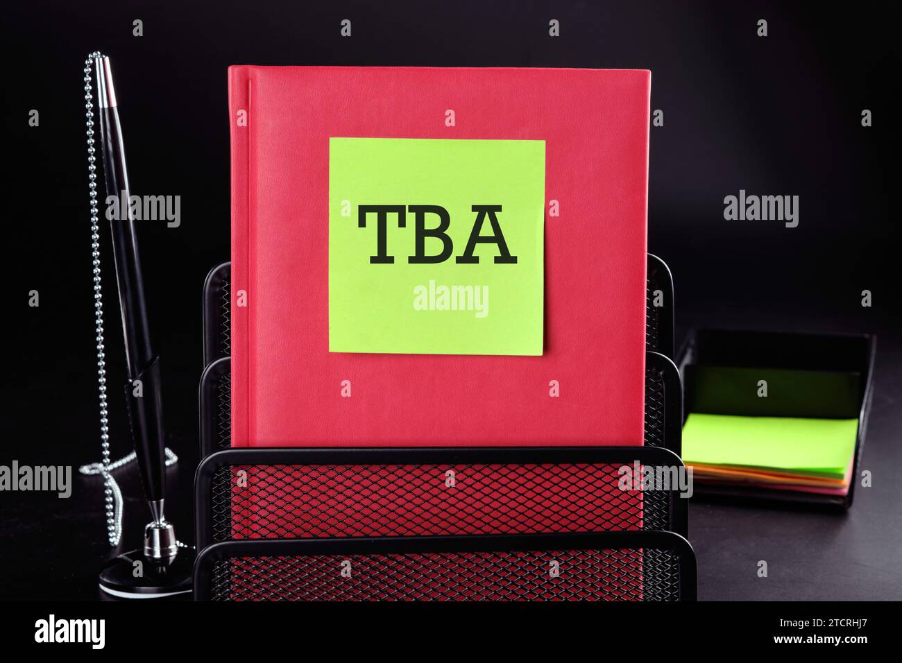 TBA Text on a yellow sticker on a red vertical notepad on a black ...
