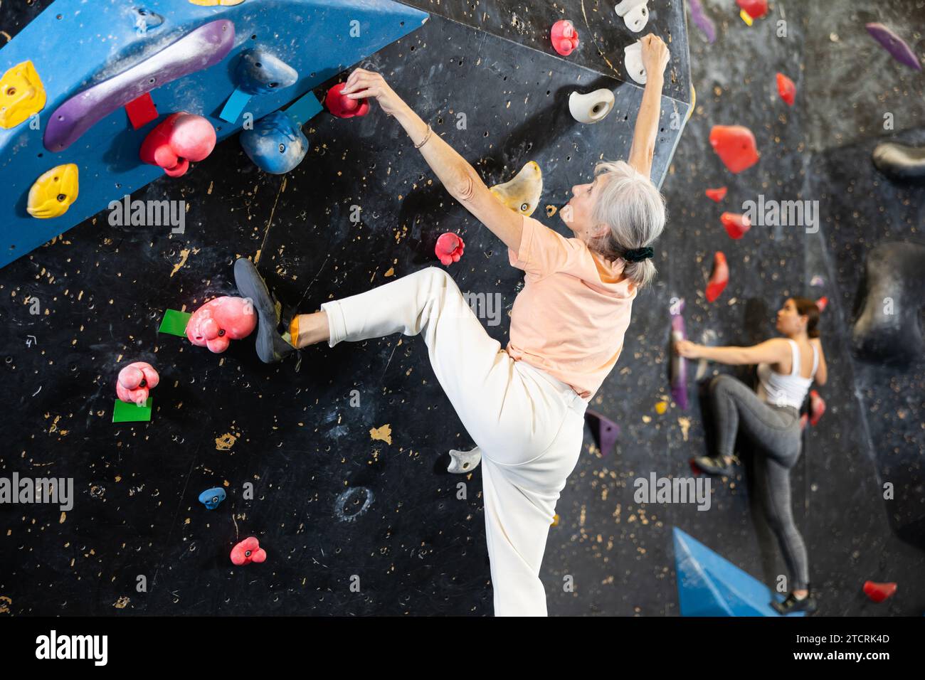 Confident mature woman scaling artificial climbing wall in climbing gym ...