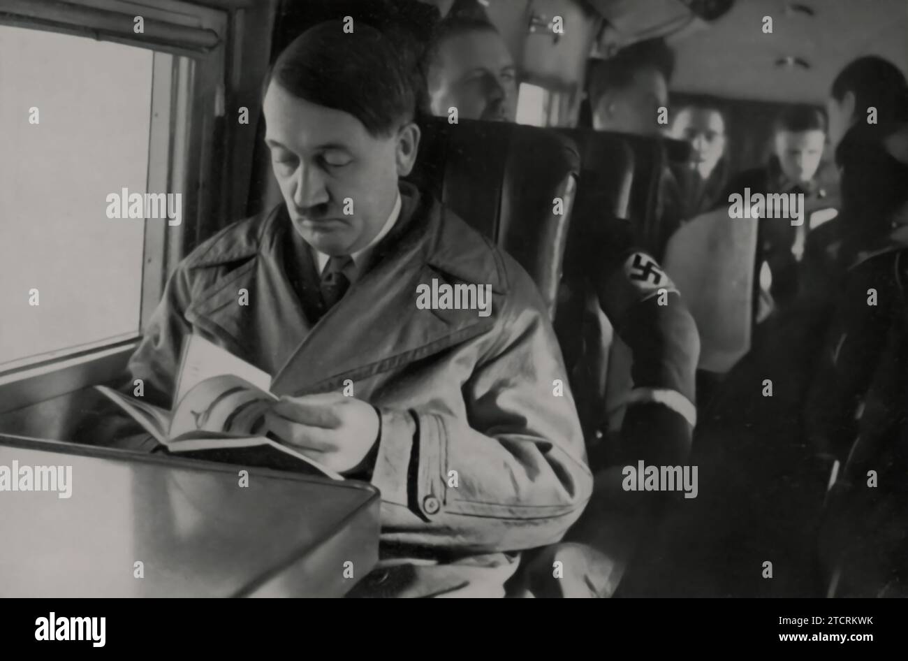 Adolf Hitler is shown seated within the confines of an aircraft, a ...