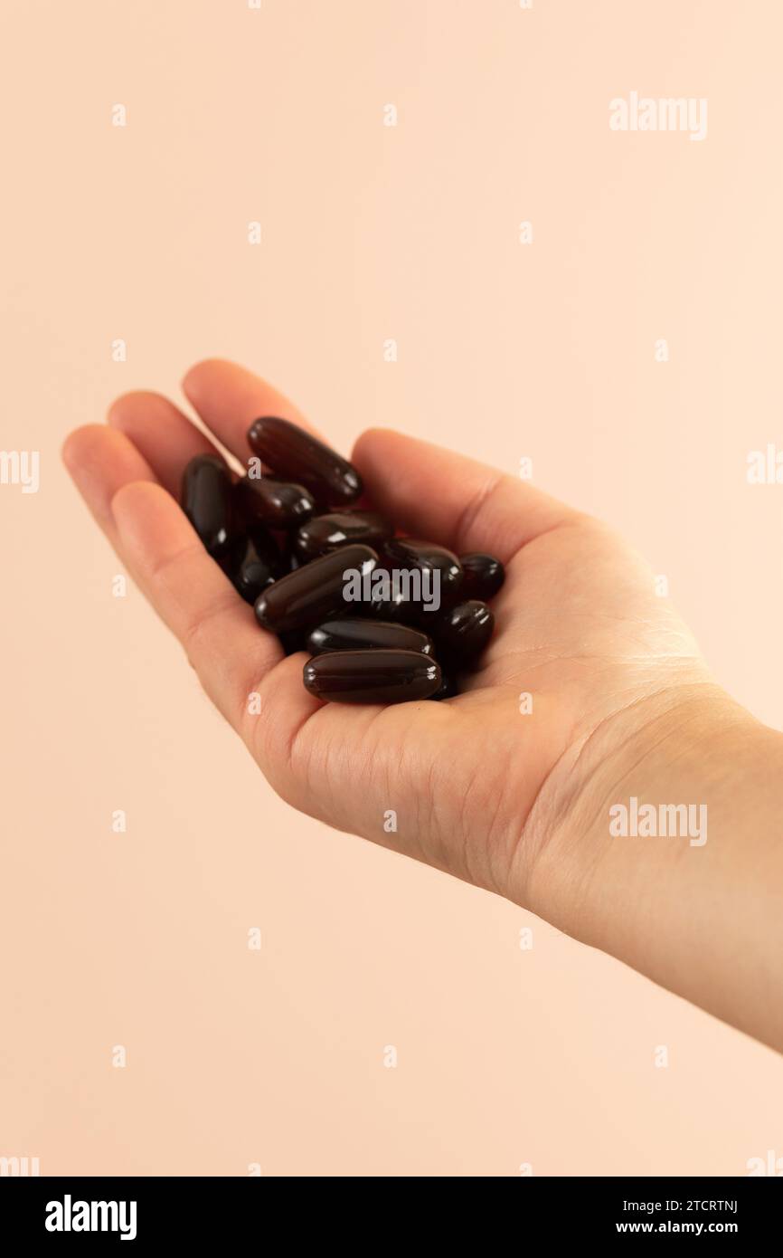 White medicinal capsules in a woman's palm on a pink background ...