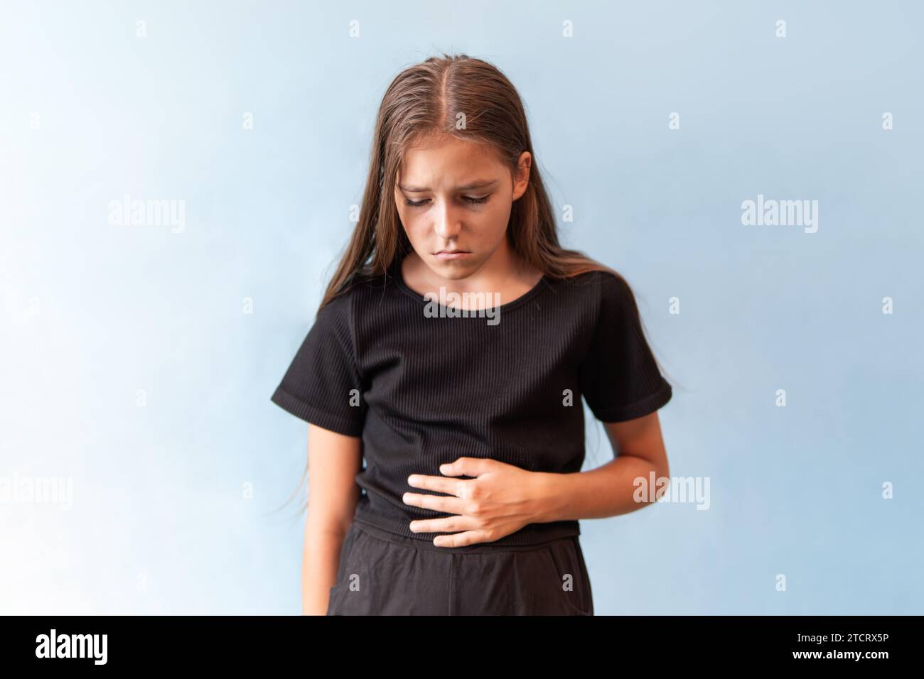 Young girl with bellyache on a blue background. A teenage girl holds ...