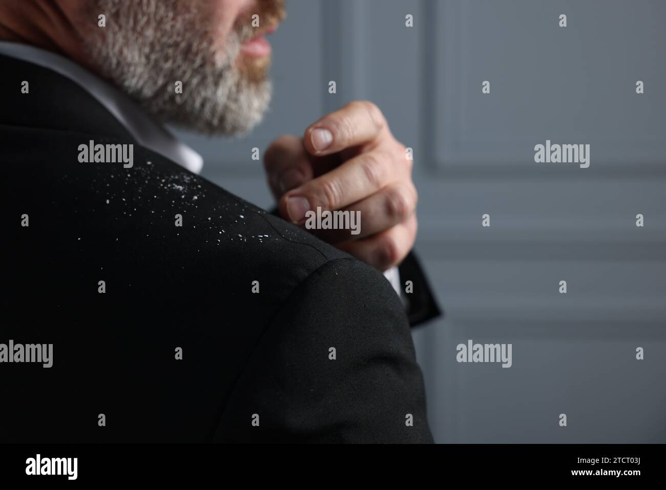 Bearded man brushing dandruff off his jacket on grey background ...