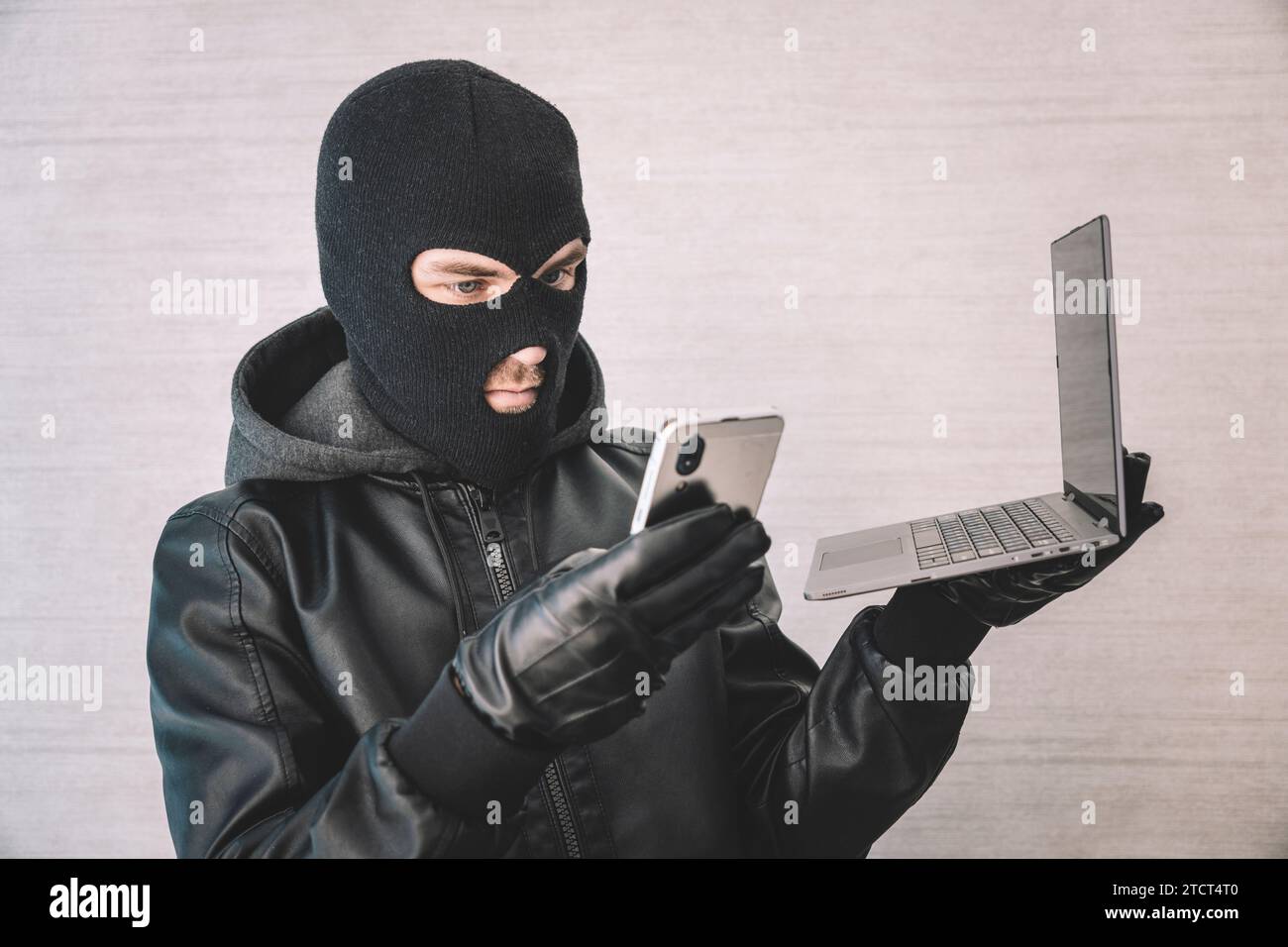 a hacker thief uses a smartphone and laptop to steal money over the ...