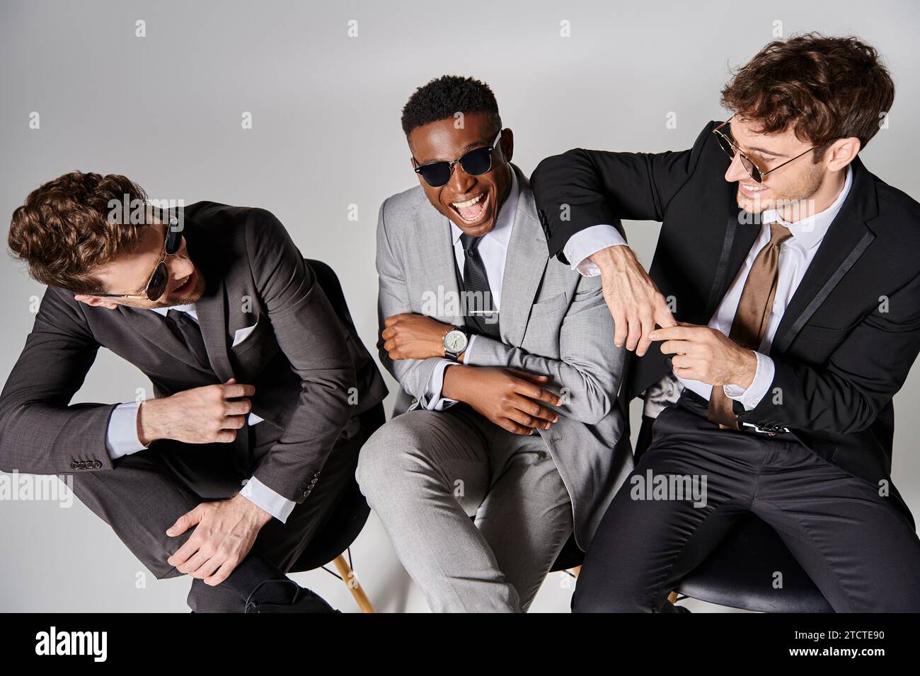 happy young multicultural men in business smart suits sitting on chairs ...