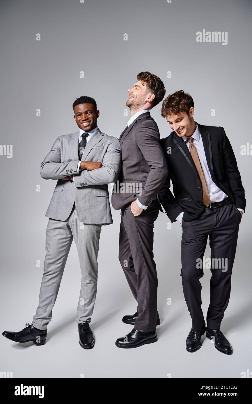 happy multiracial friends in business casual outfits posing on gray ...