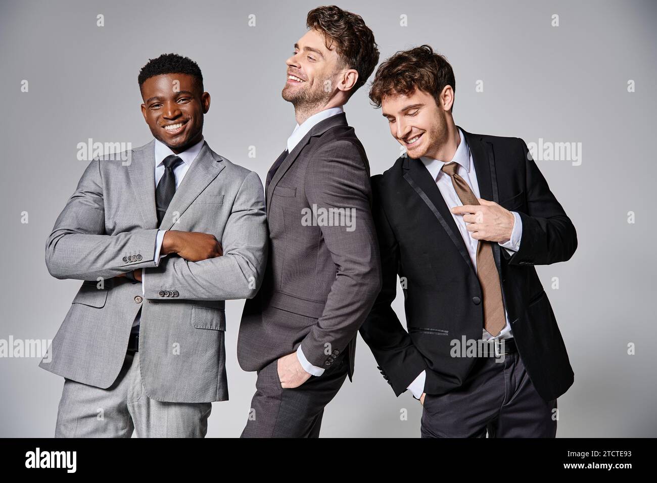 happy multicultural friends in business casual outfits posing on gray ...