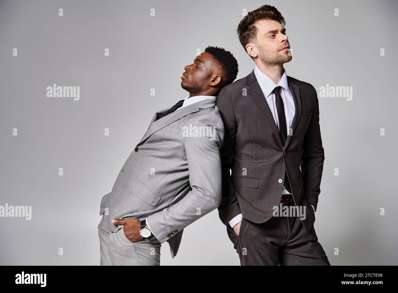 two handsome stylish multicultural male models in business smart attires posing on gray backdrop ...
