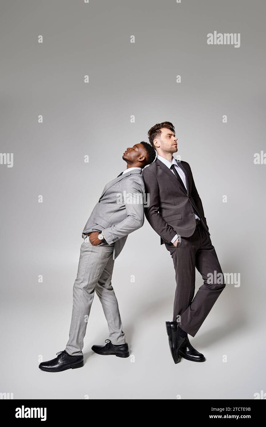 two handsome trendy multicultural male models in business smart attires posing on gray backdrop ...