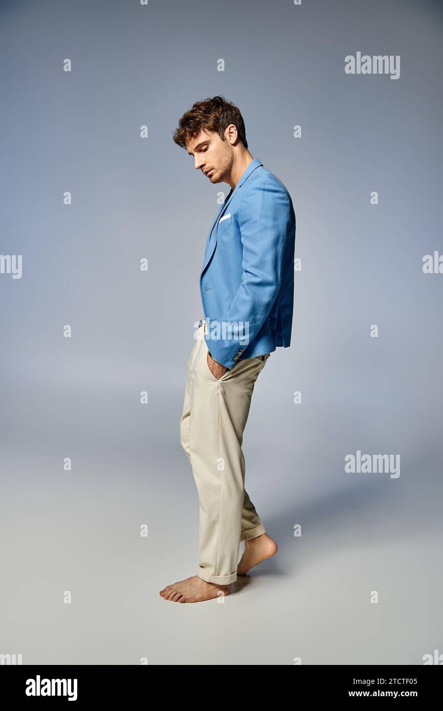 young handsome man in vibrant unbuttoned blue jacket posing on gray ...