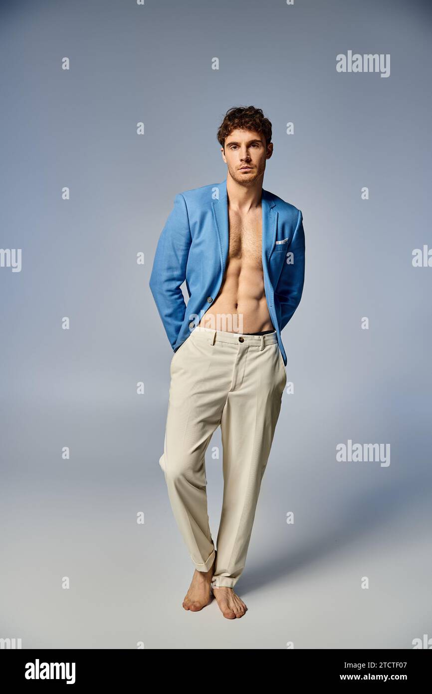 young attractive man in vibrant unbuttoned blue jacket posing on gray ...