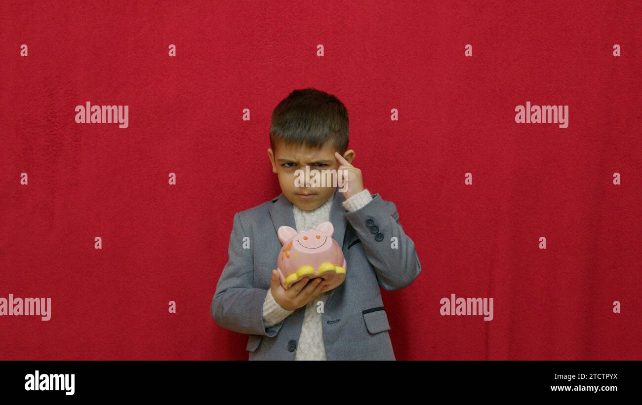 Cute boy in business suit holding piggy bank and getting an idea how to ...