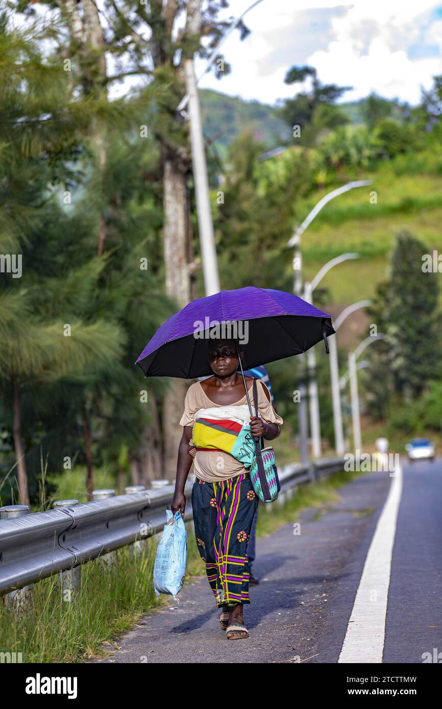 Woman walking along an uphill road carrying an umbrella in western ...