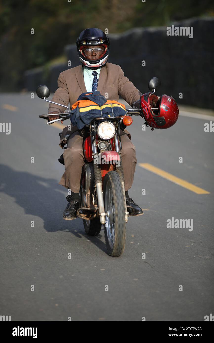 Man in a suit riding a motorcycle on a road in western Rwanda Stock ...