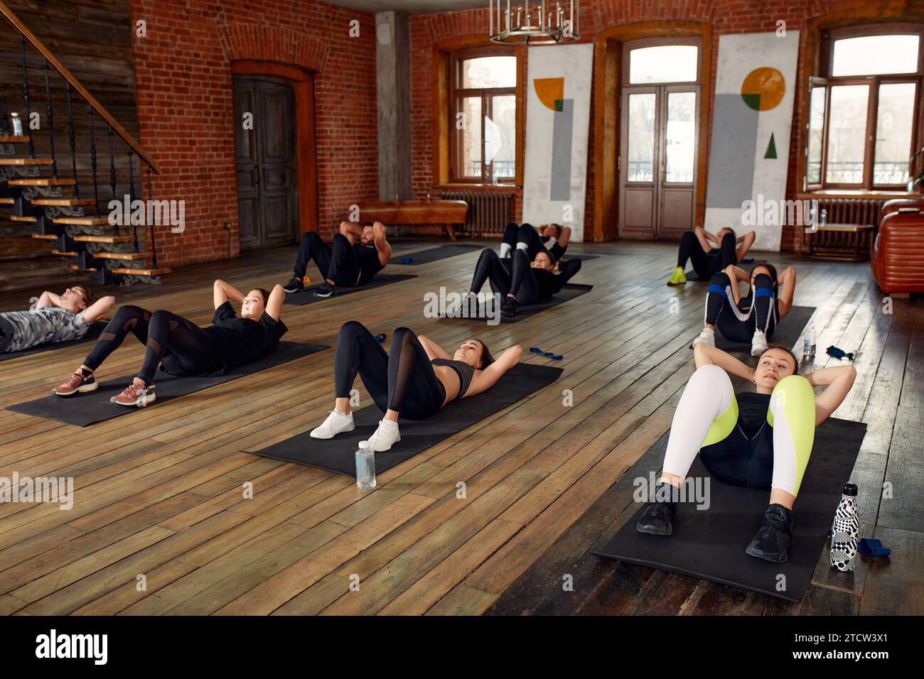 Group of athletic adult men and women performing sit up exercises to ...