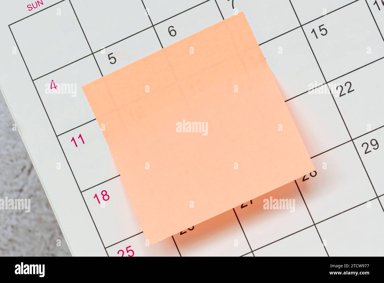 Orange paper sticky note and stuck to a calendar background. Reminder ...