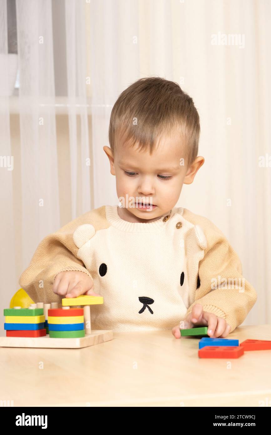 A two-year-old boy plays with wooden toys to develop logic and motor ...
