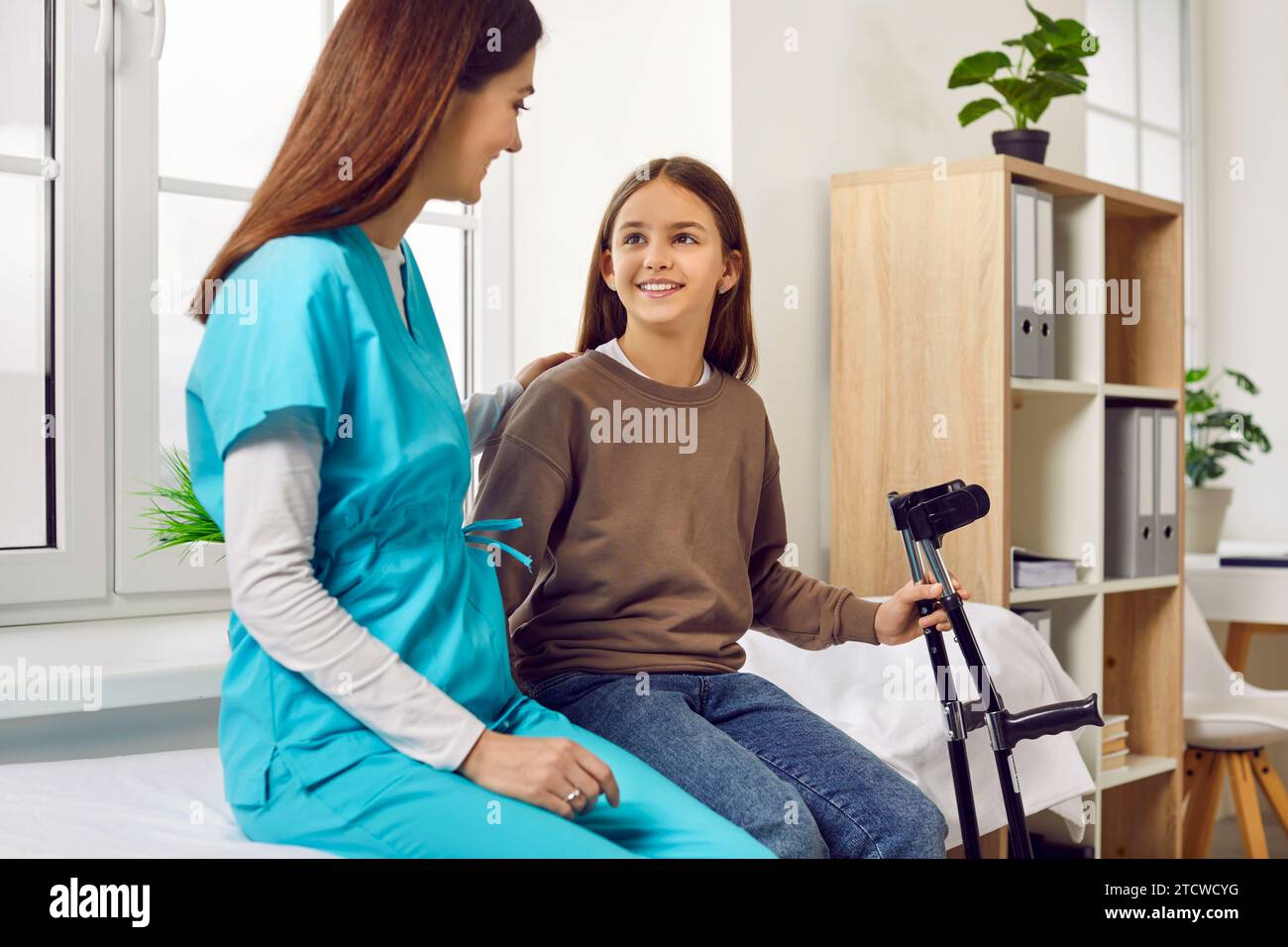 Smiling doctor or nurse supporting her child patient with leg injury ...