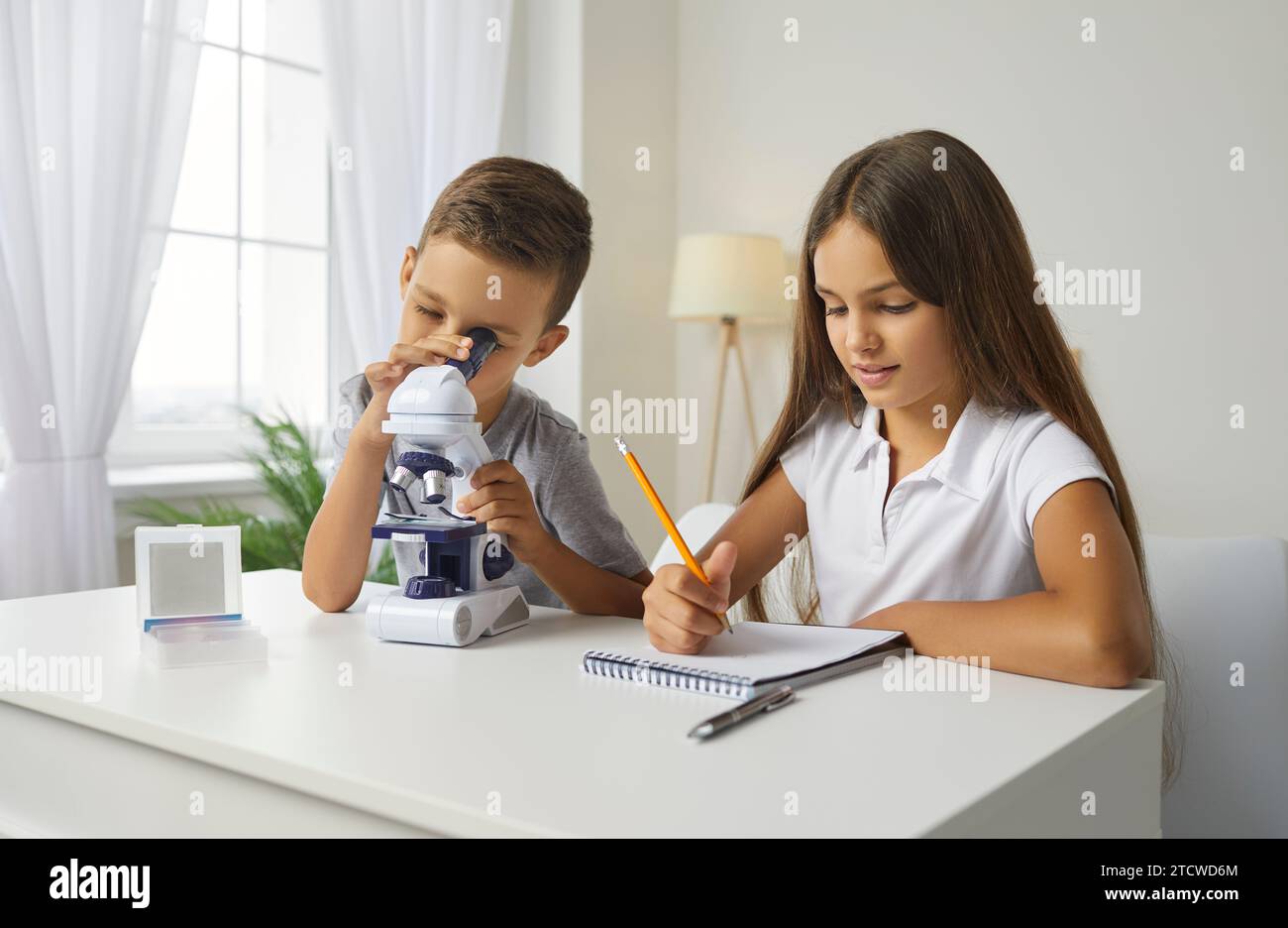 Two little school children take notes while looking at something under ...