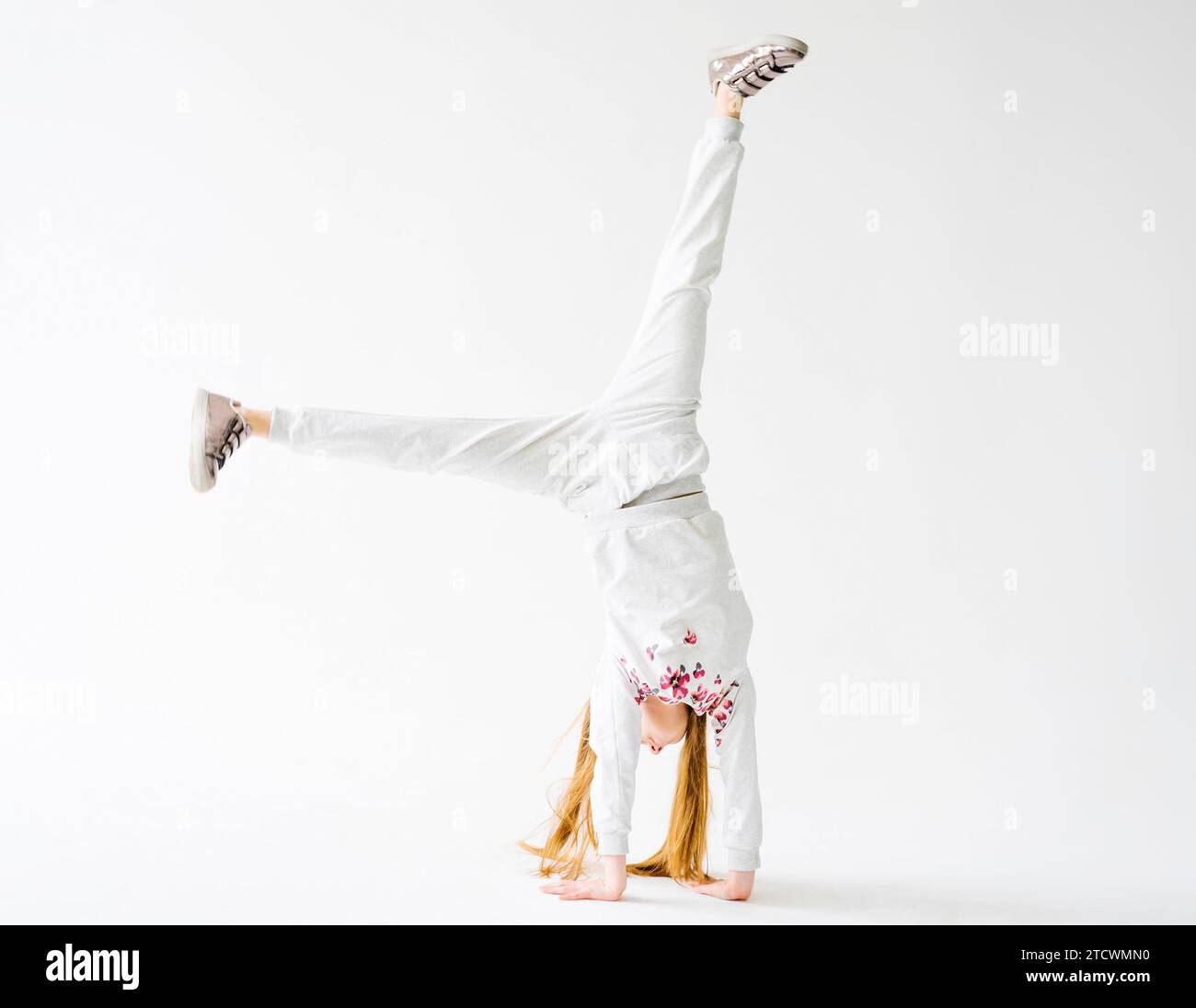 Active little girl in grey sport clothes doing a handstand on white ...