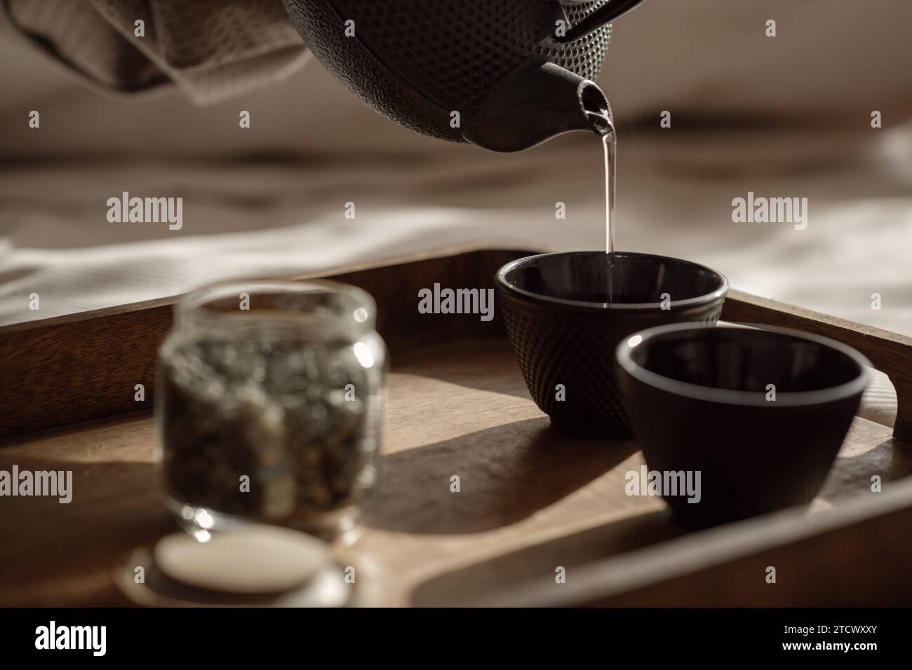 Black cast iron tea pot with herbal tea set up on wood tray on the bed ...