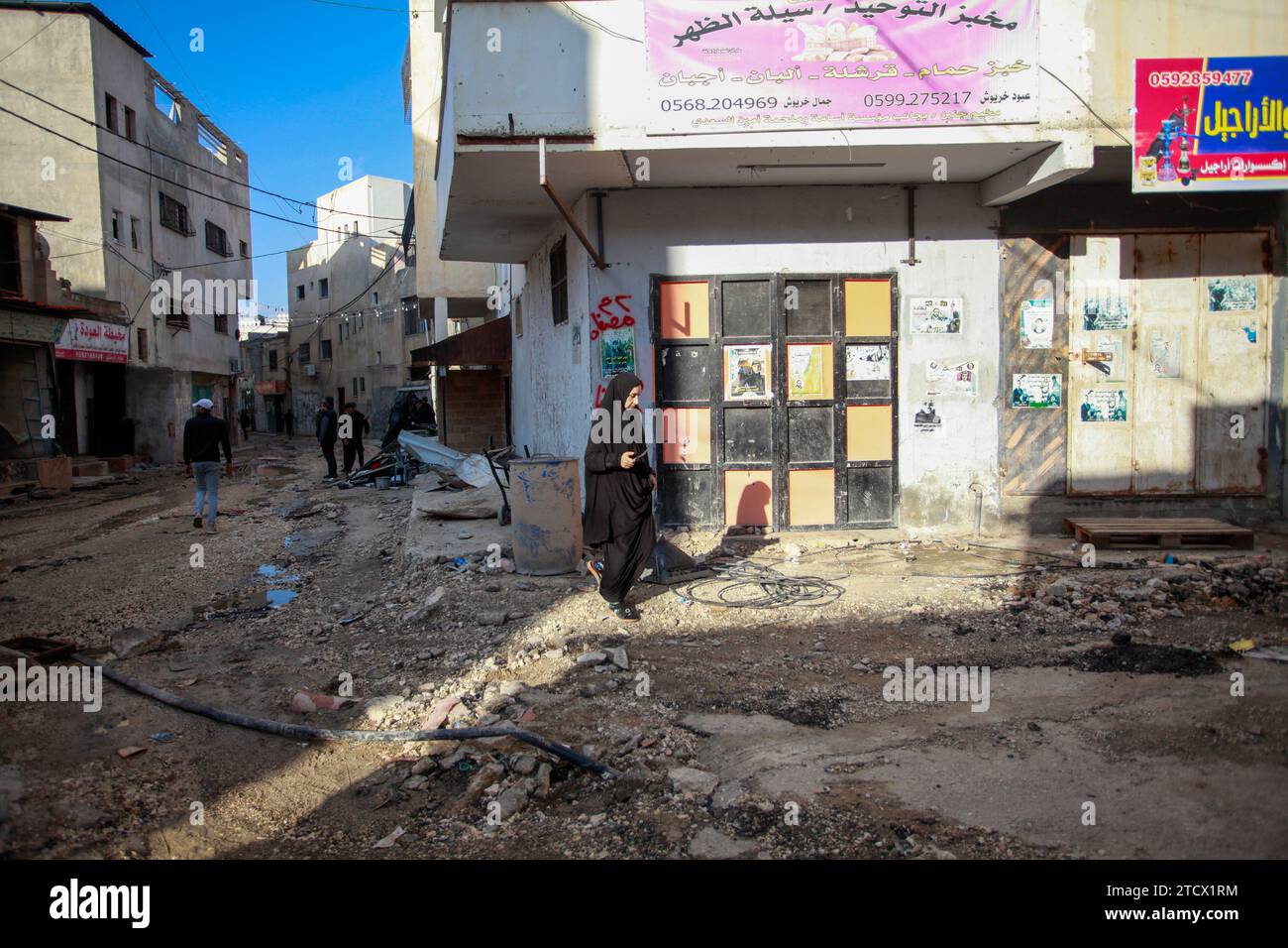 Jenin, Palestine. 14th Dec, 2023. Palestinians walk past damaged street ...