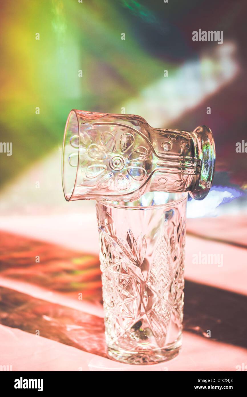 Faceted glasses cast a shadow on a multicolored rainbow background. Nostalgic drink ware for ...