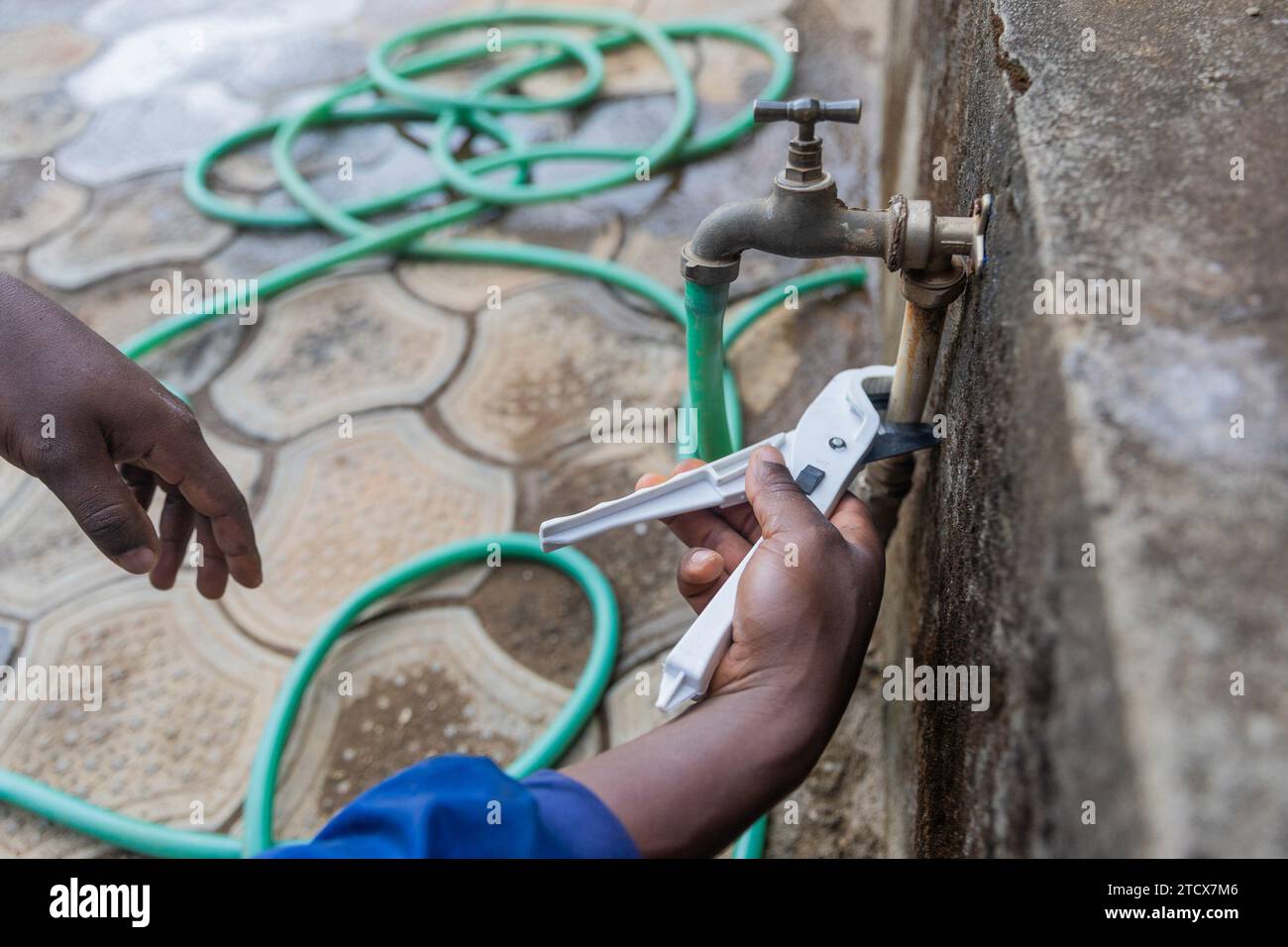 Close-up of the hands of an African plumber fixing the outside tap ...