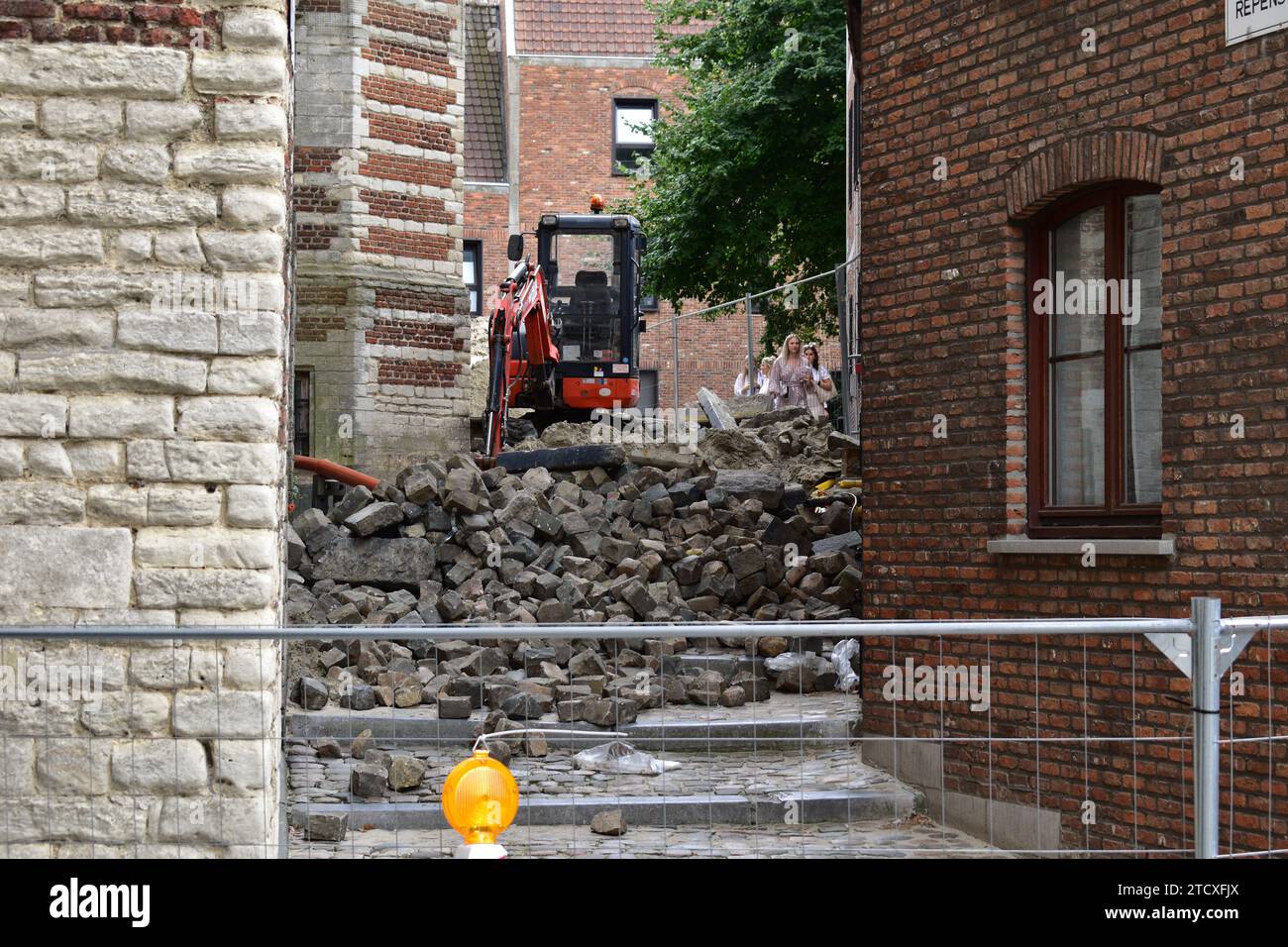 Small excavator stands on a pile of cobblestone rubble in a small alley ...