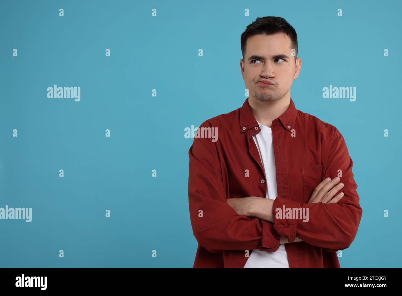 Resentful man with crossed arms on light blue background, space for ...