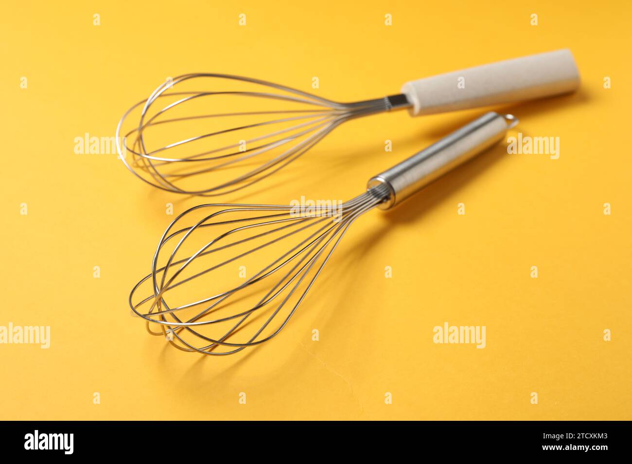 Two metal whisks on yellow background, closeup. Kitchen tool Stock ...
