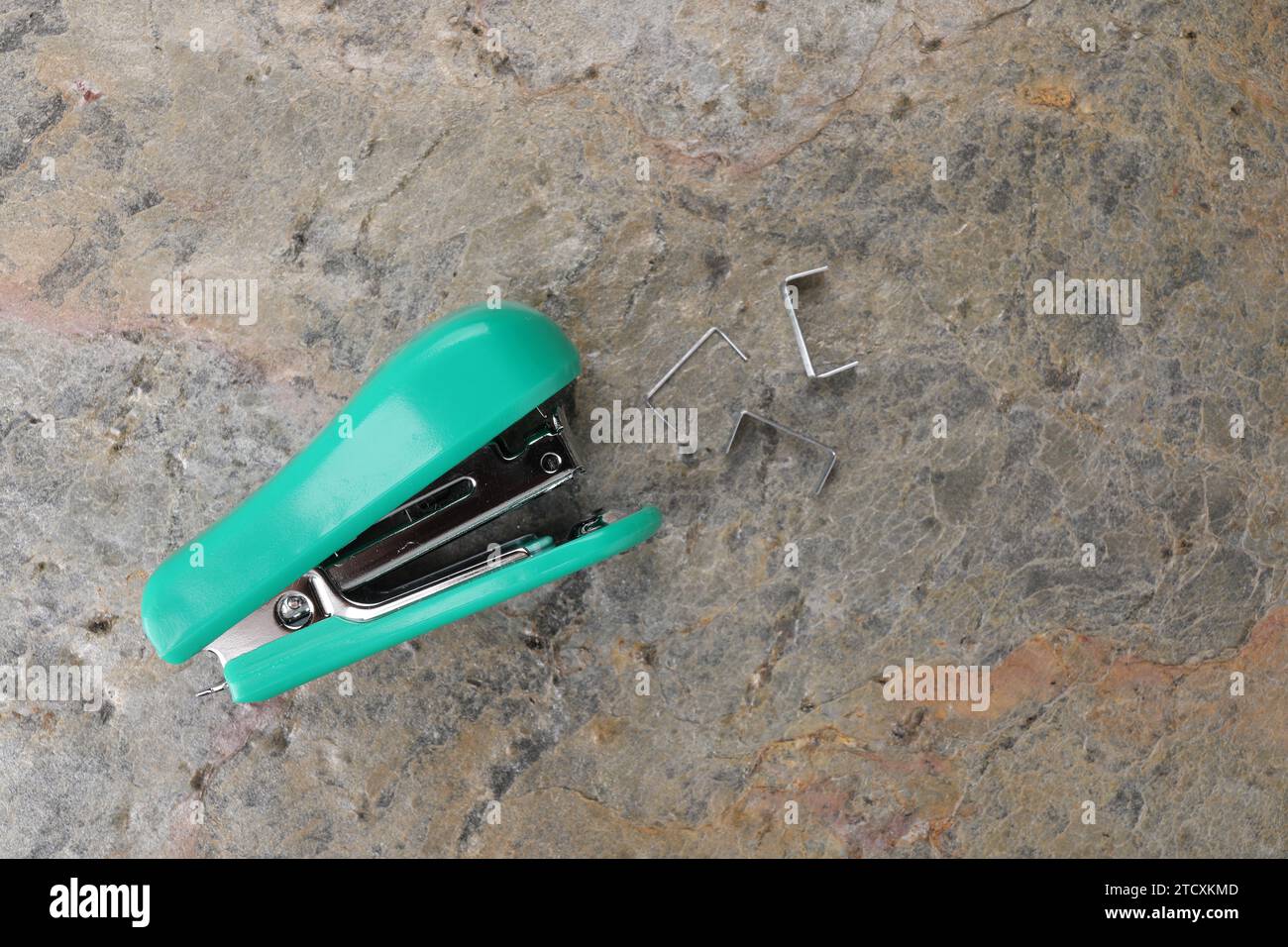 Turquoise stapler with staples on stone textured surface, top view ...