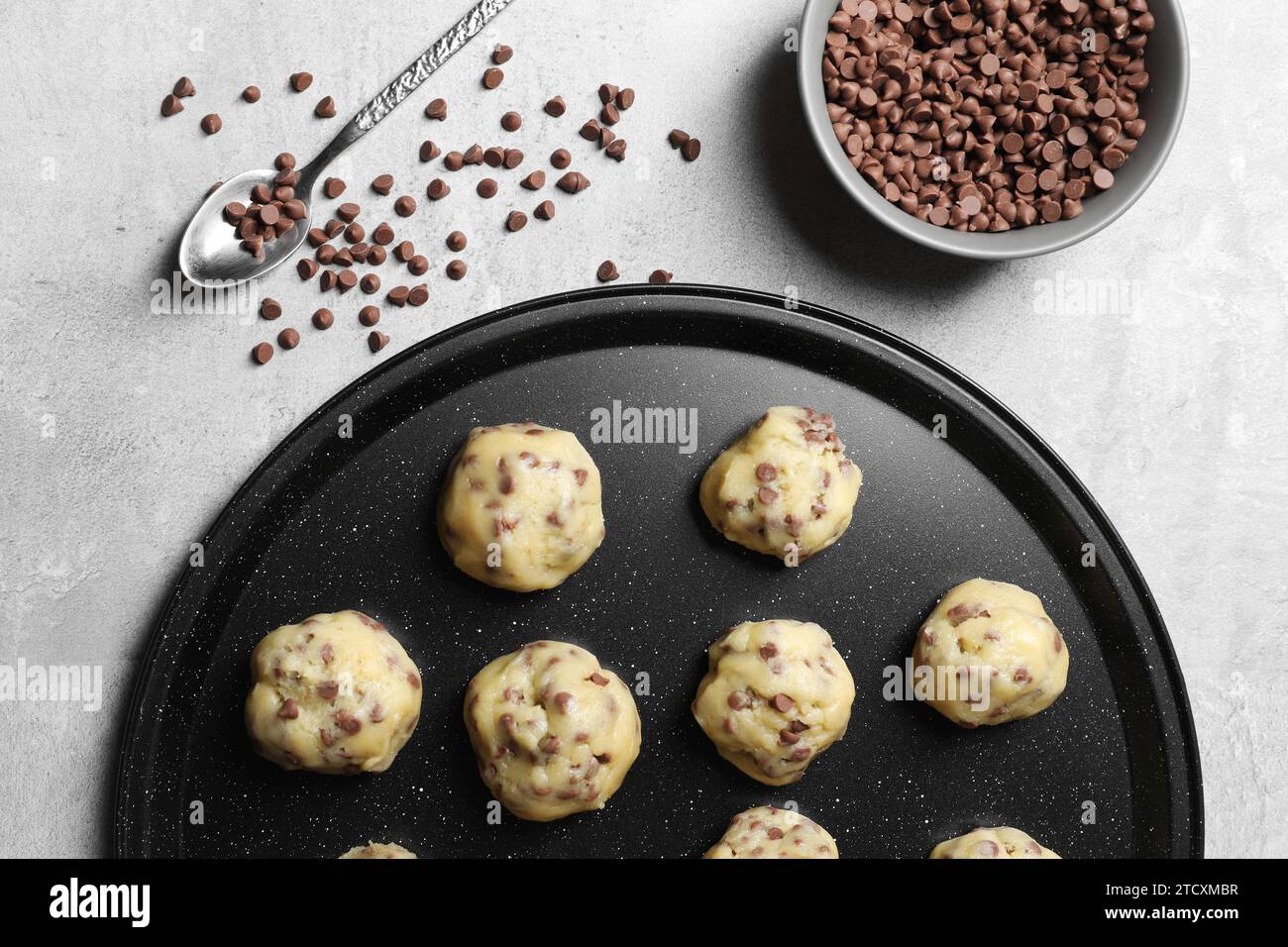 Tray with raw chocolate chip cookie balls and spoon on gray table, flat ...