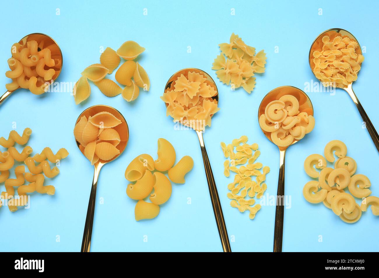Spoons with different types of pasta on light blue background, flat lay ...