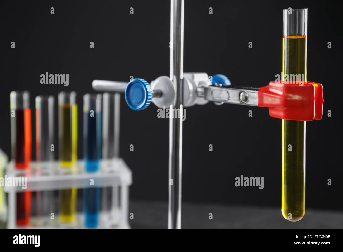 Retort stand and test tube with liquid on black background, closeup ...