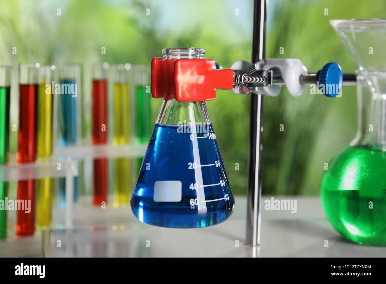Retort stand and laboratory flask with liquid on table against blurred ...