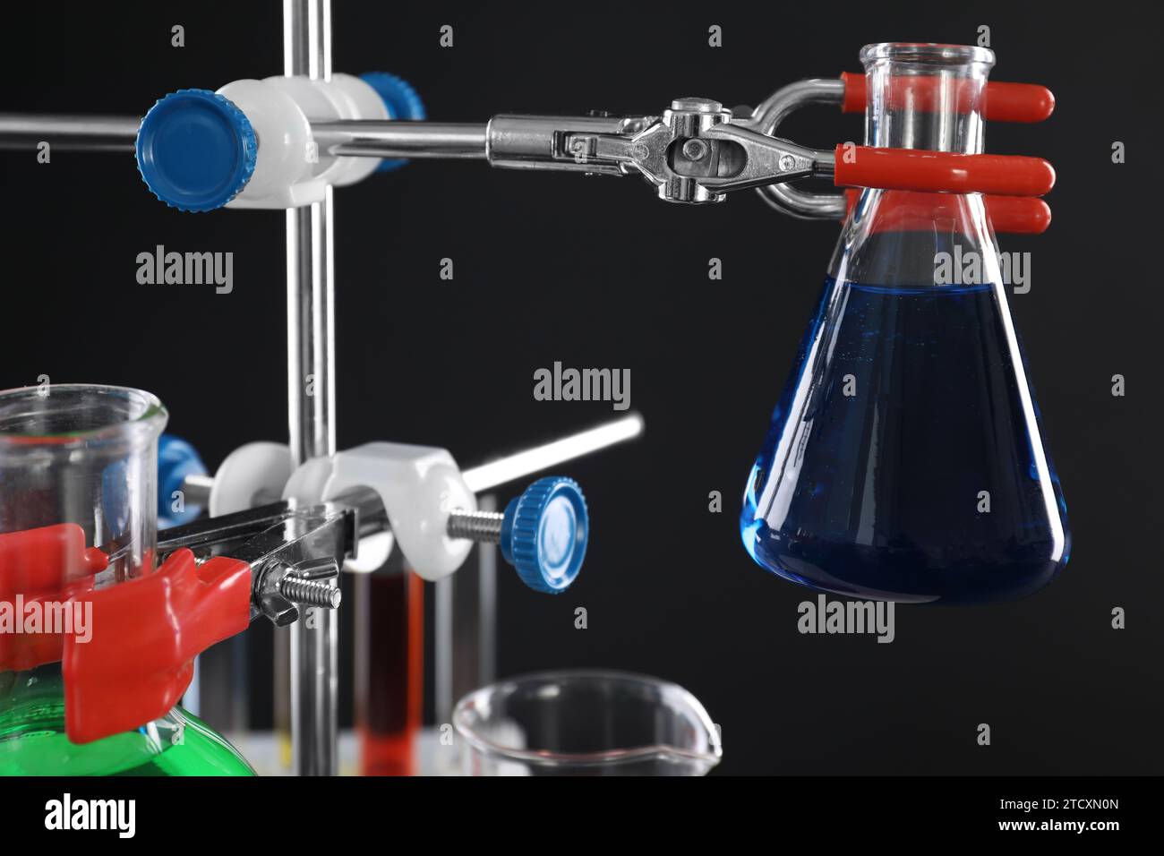 Retort stand and laboratory glassware with liquids on black background ...