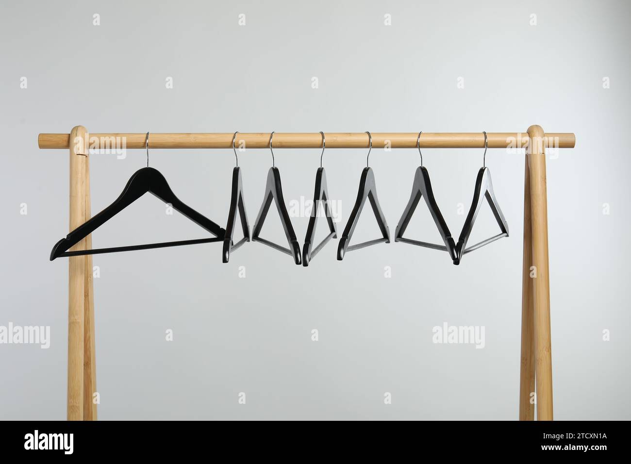 Black clothes hangers on wooden rack against light grey background ...