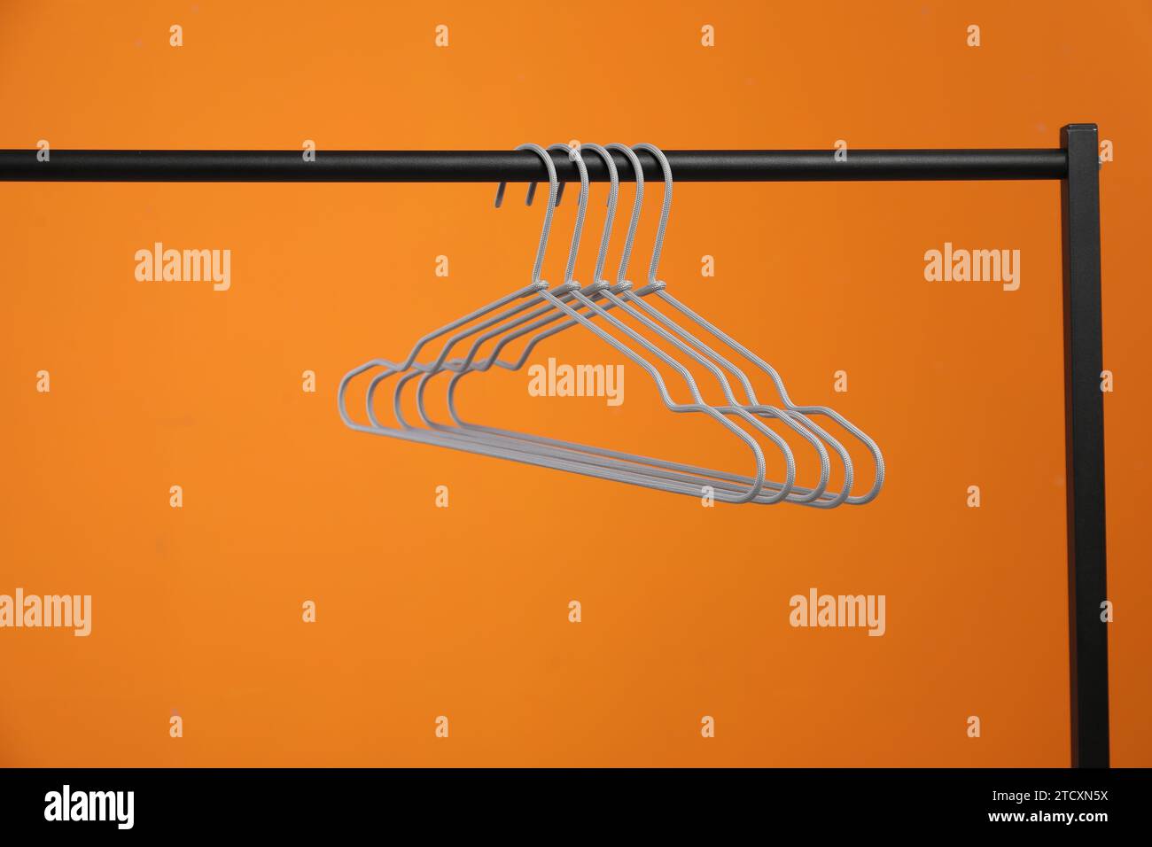 Empty clothes hangers on rack against orange background Stock Photo - Alamy