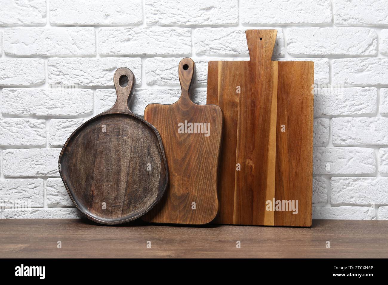 Different cutting boards on wooden table near white brick wall Stock ...