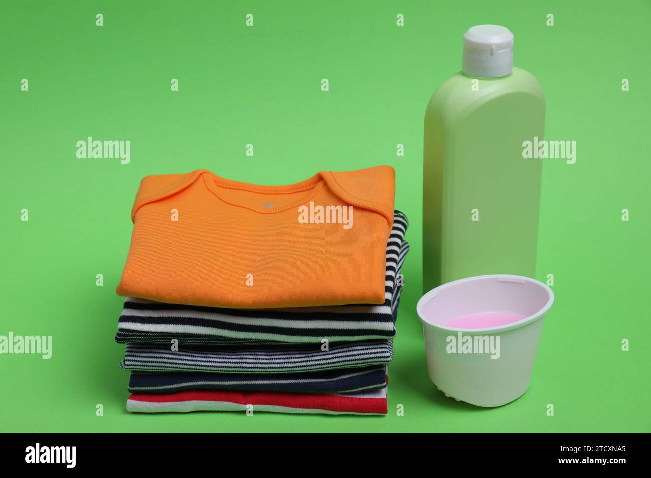 Stack of baby clothes and laundry detergents on light green background ...