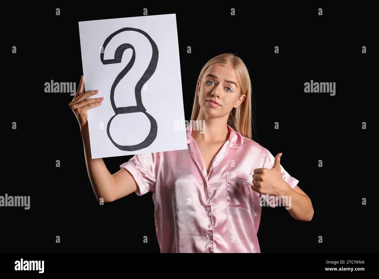 Young woman in pajamas holding paper with question mark and showing ...