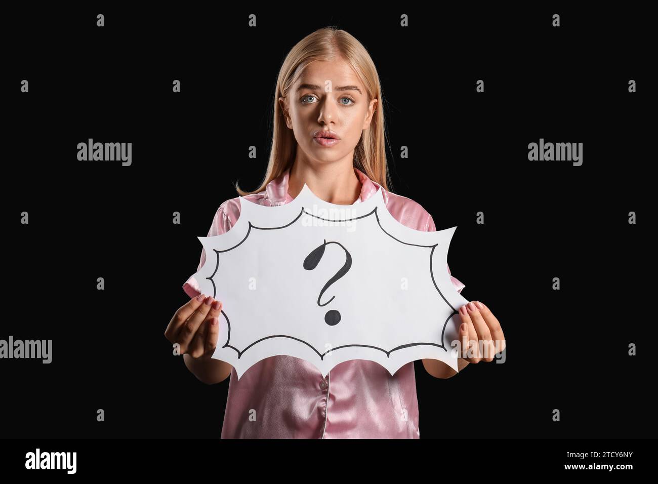 Young woman in pajamas holding speech bubble with question mark on ...