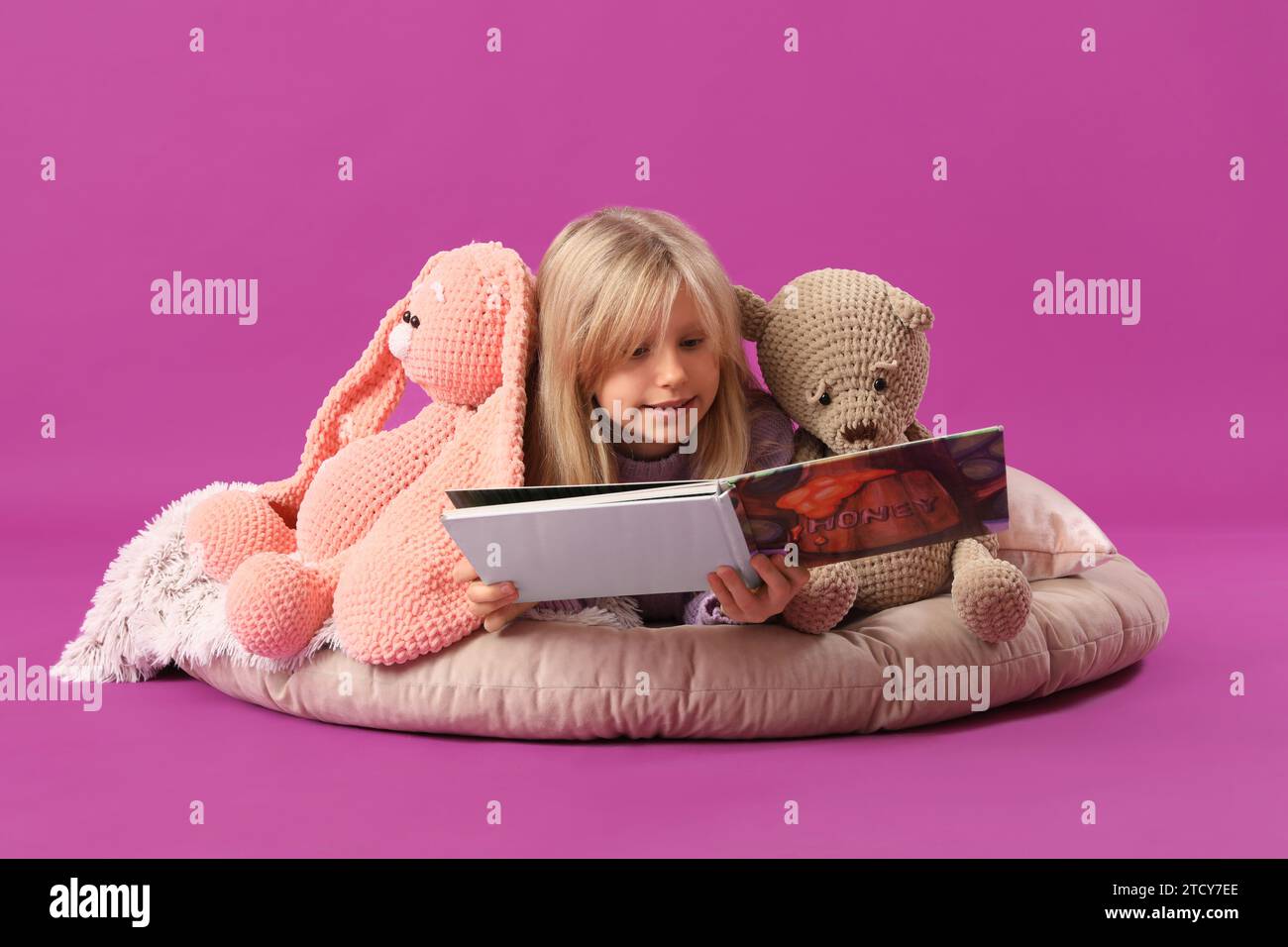 Cute little girl with plush toys reading fairy tale book on purple ...