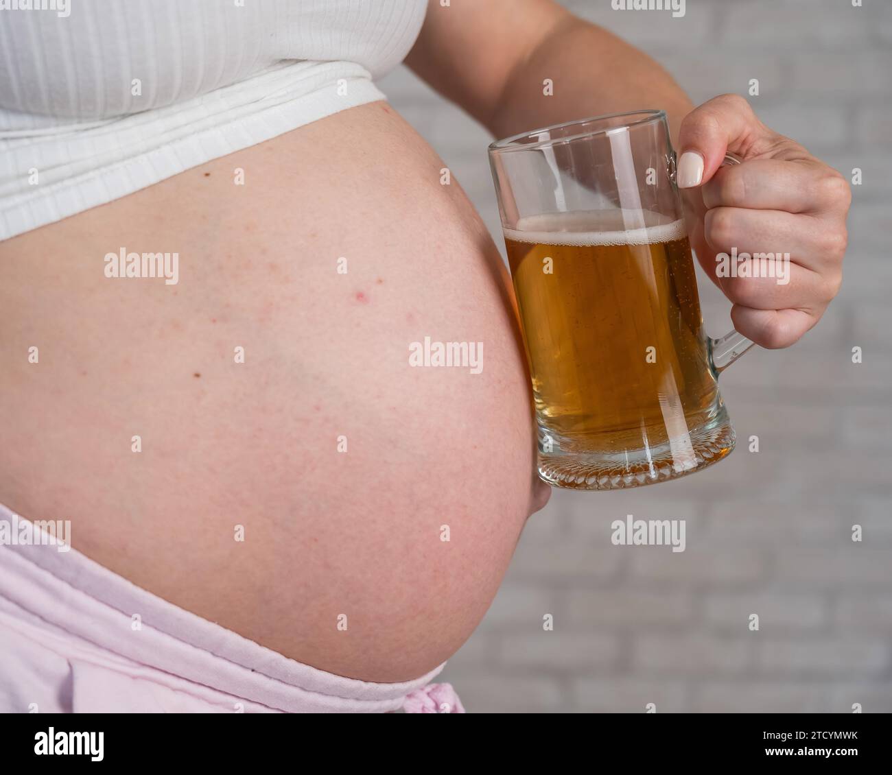 Faceless pregnant woman with rash on stomach holding glass of beer ...