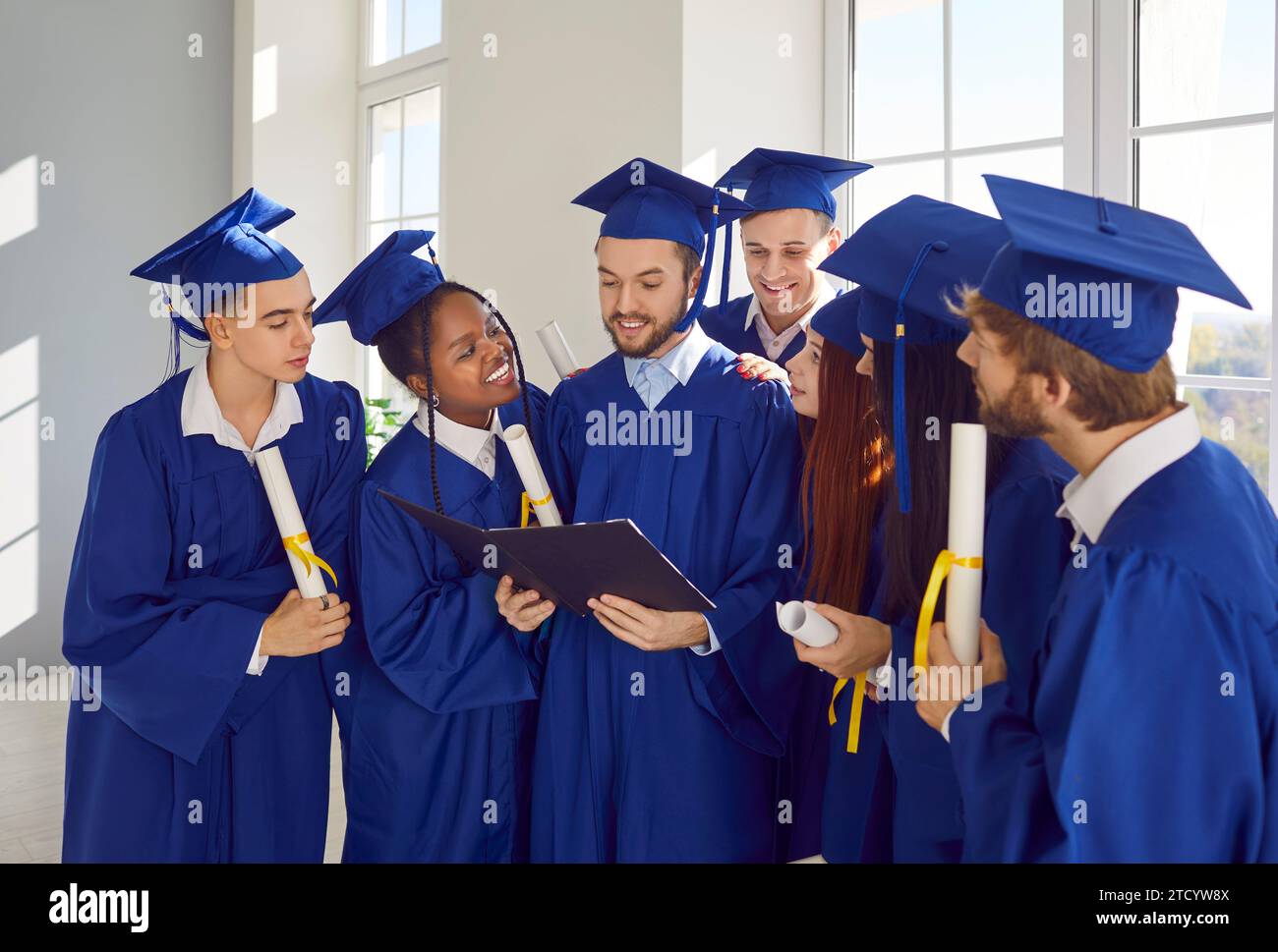 Happy graduate students in blue graduation robes looking to diploma of ...