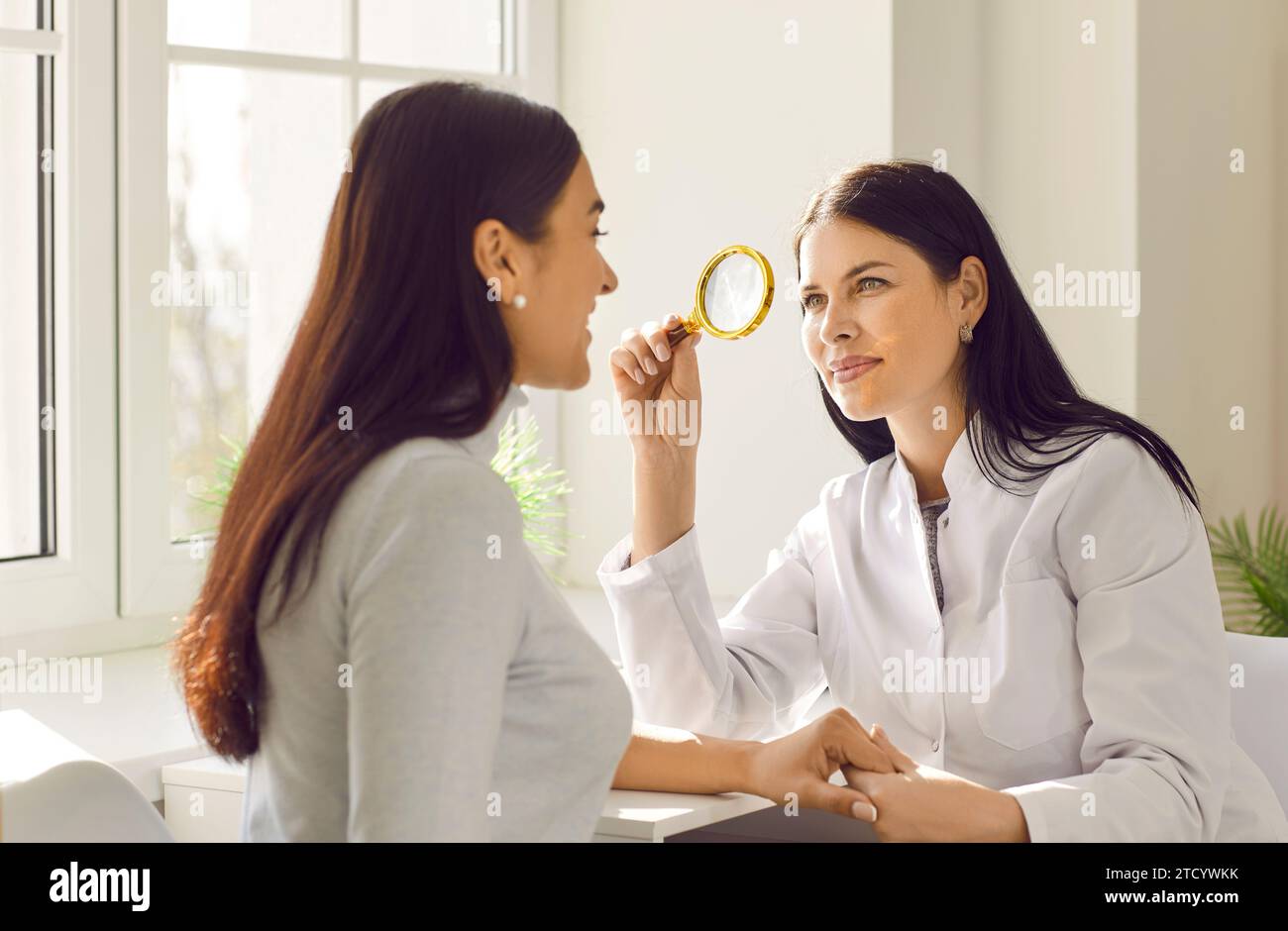 Female friendly doctor examining face skin of young smiling woman ...