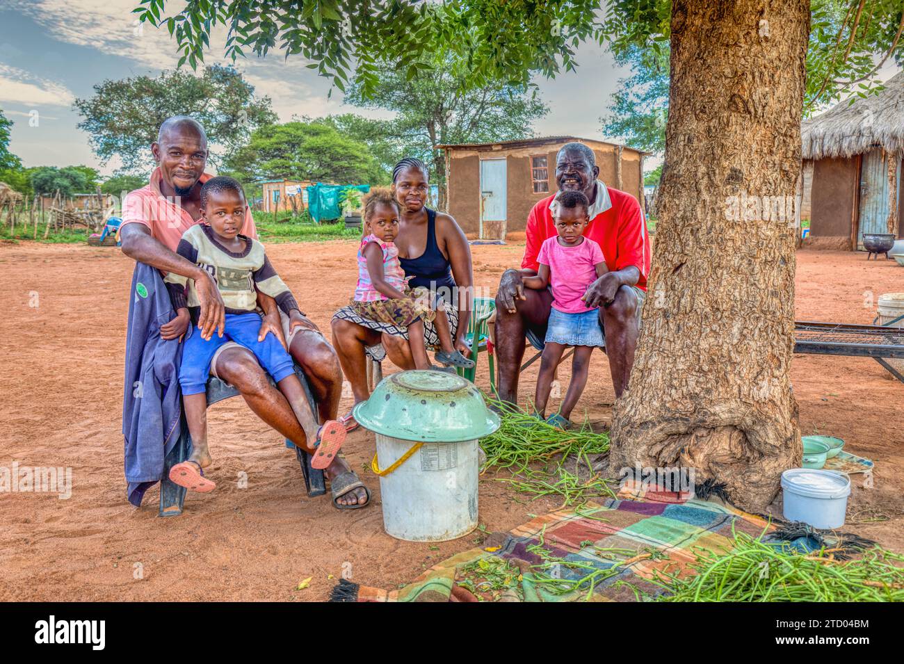 village african family, sited in the yard in front of the house, hut with thatched roof in the ...