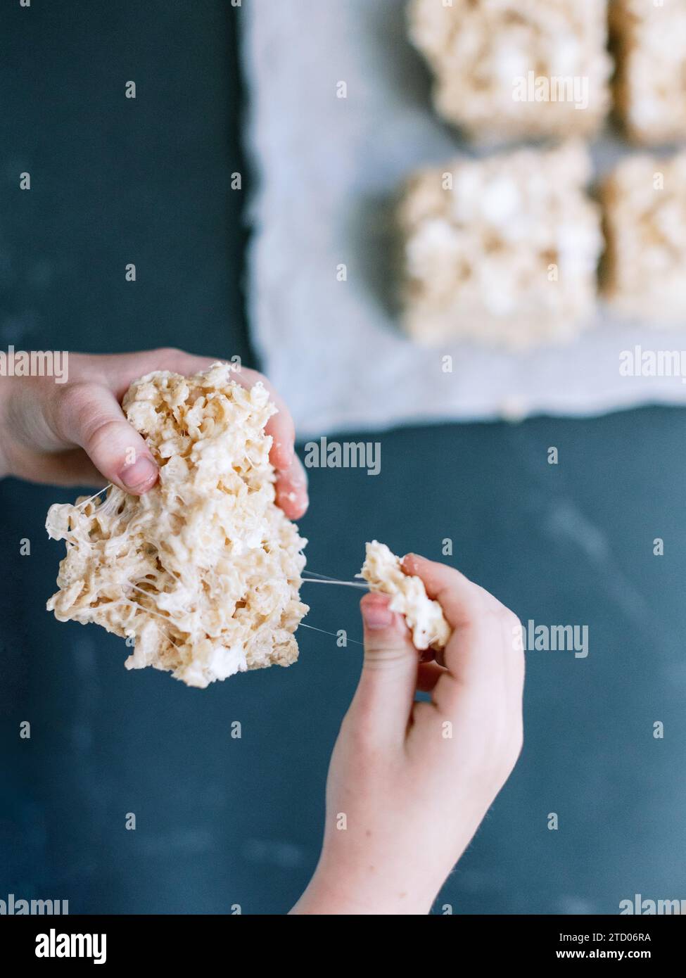 overhead shot of hands pulling gooey rice krispie on blue background ...